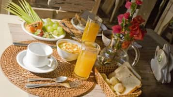 Uma mesa de café da manhã com uma travessa de frutas, um copo de suco de laranja, uma xícara e um pequeno vaso com flores.