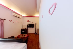Quarto de hotel com cama, escrivaninha, cadeira, televisão e parede decorada com corações.