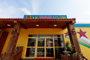 Um edifício com fachada amarela, entrada de madeira e placa com texto vermelho e amarelo.