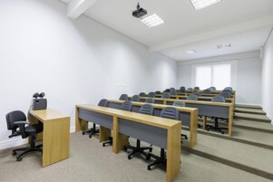 Uma sala de conferências com fileiras de mesas e cadeiras, um projetor e um quadro branco.