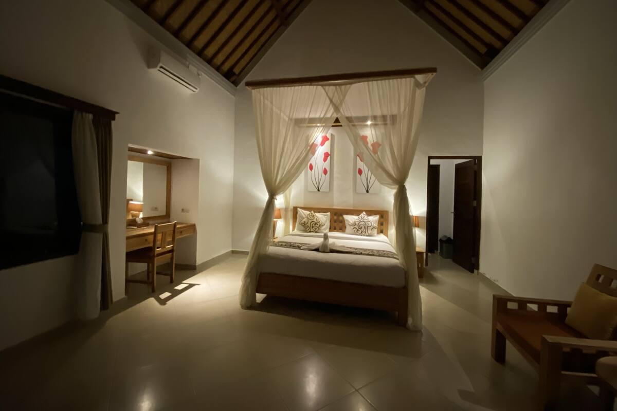 Quarto com cama de dossel, uma escrivaninha e uma cadeira.
