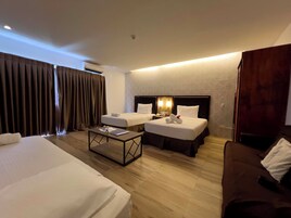 Quarto de hotel com duas camas, um sofá, uma mesa de centro e uma janela grande com cortinas.
