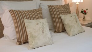 Uma cama bem arrumada com almofadas listradas e florais, uma luminária de cabeceira e um vaso com flores em uma mesa de cabeceira.