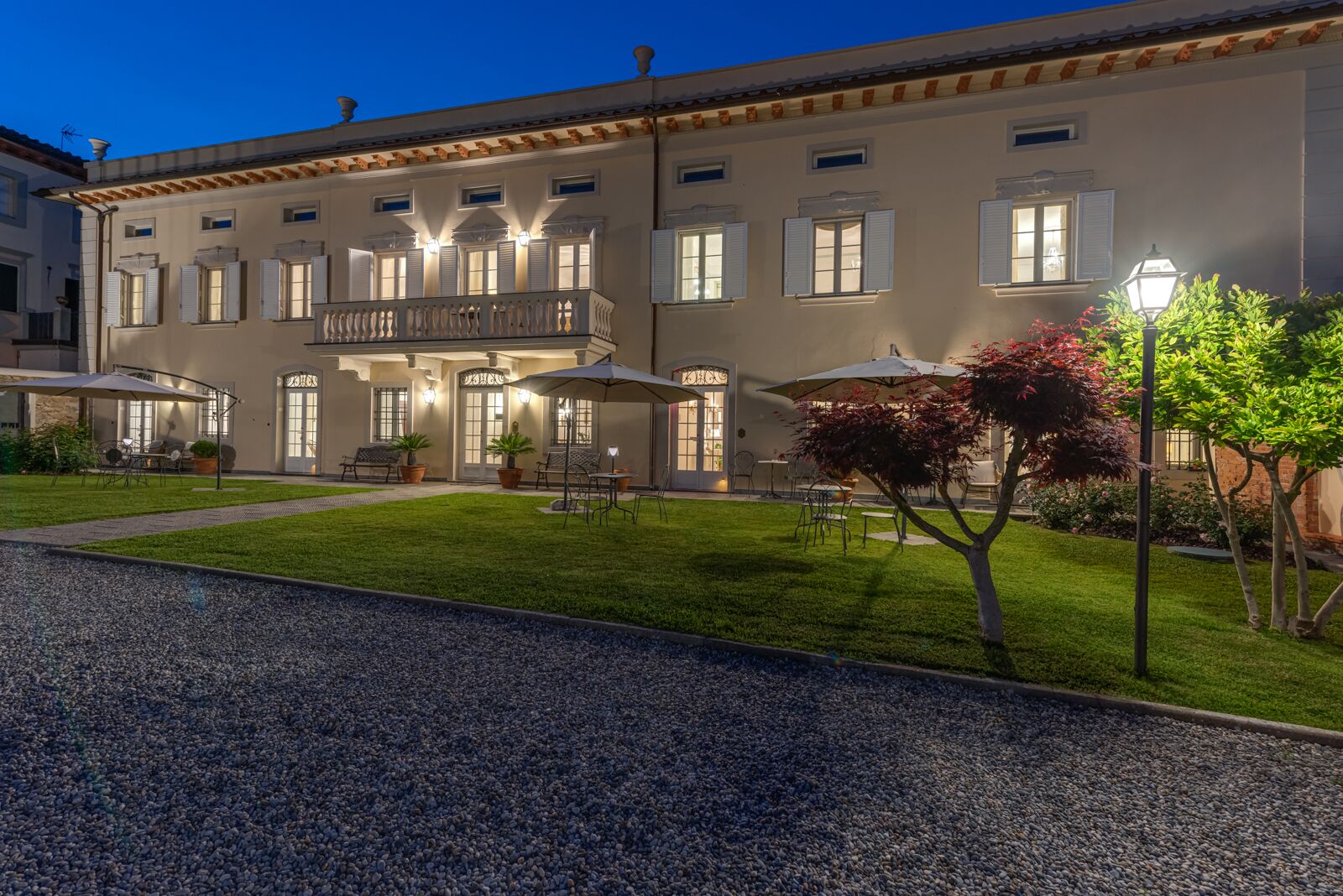 Um hotel com entrada bem iluminada, área de estar externa e um caminho de acesso de cascalho.