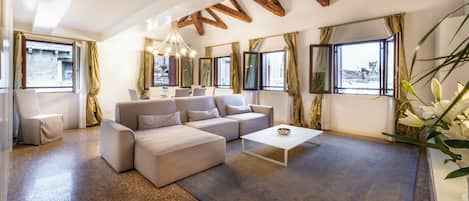Uma sala de estar espaçosa com um sofá grande, uma mesa de centro e vista para a cidade através de amplas janelas.