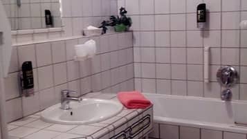 Casa de banho com paredes e chão em azulejo branco, uma pia com espelho, sanita e banheira.