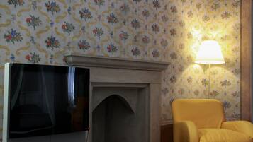Um quarto com televisão, lareira, poltrona amarela e papel de parede floral.