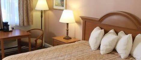 Quarto de hotel com uma cama, duas luminárias de cabeceira, uma escrivaninha com cadeira e um quadro na parede.