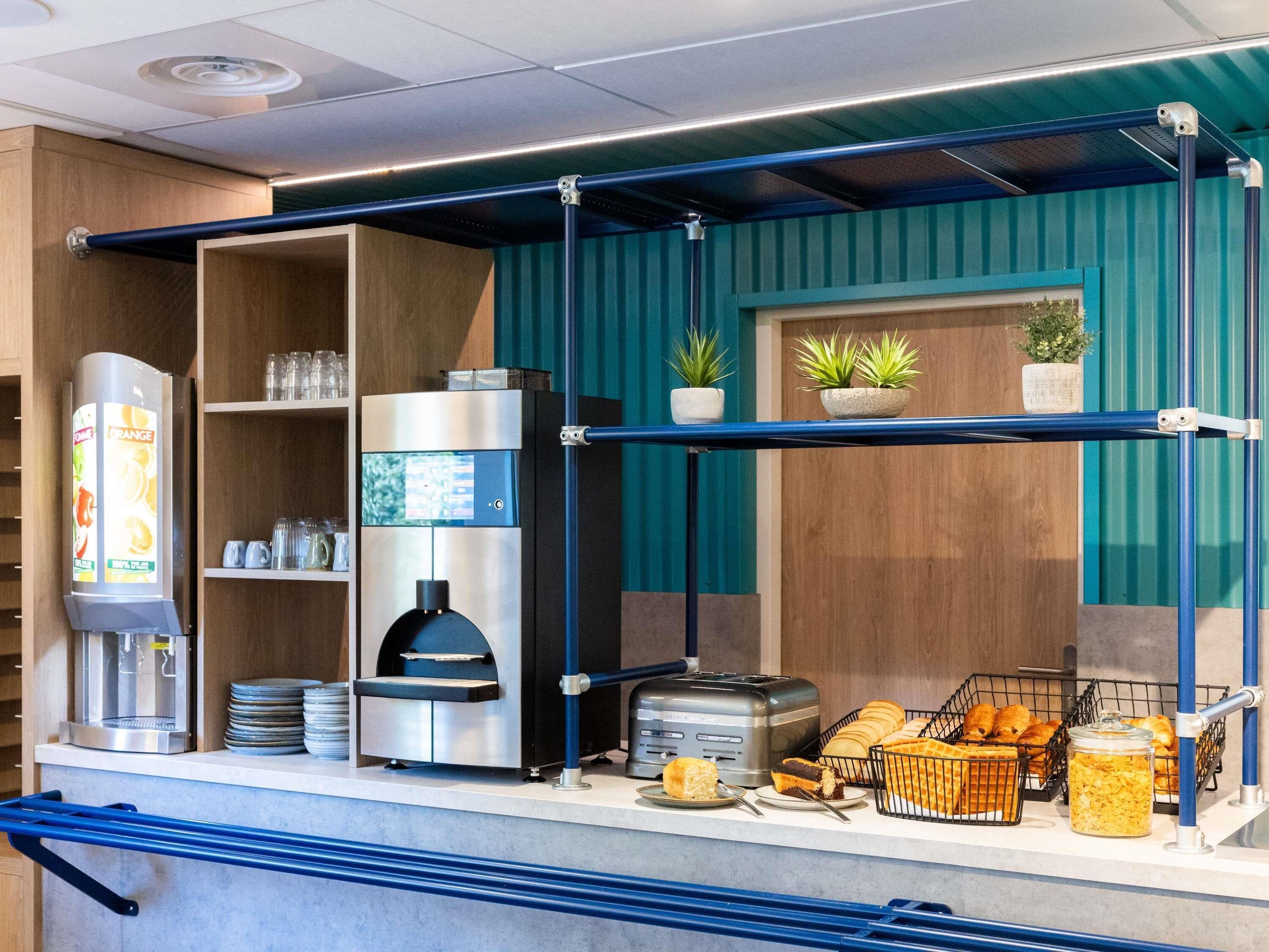Uma estação de café da manhã com serviço livre, incluindo máquina de café, torradeira e diversas opções de alimentos.
