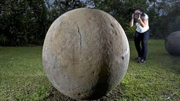 Uma grande esfera de pedra em uma área gramada, com árvores ao fundo.