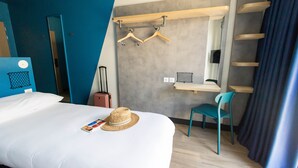 Quarto de hotel com cama, escrivaninha, cadeira, cabideiro e mala.