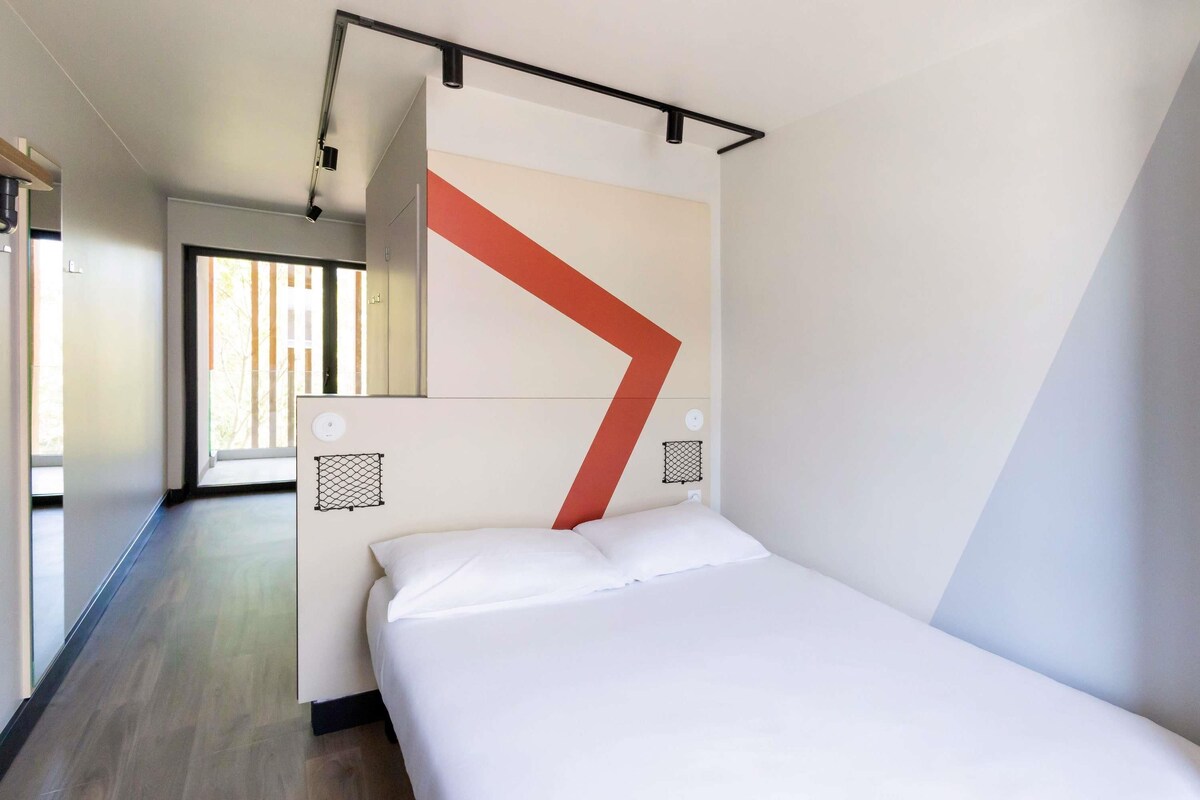 Quarto de hotel moderno com uma cama grande, um design geométrico na parede e vista para o exterior.