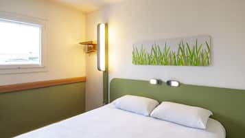 Quarto de hotel com cama, janela, luminária na parede e pintura de relva.