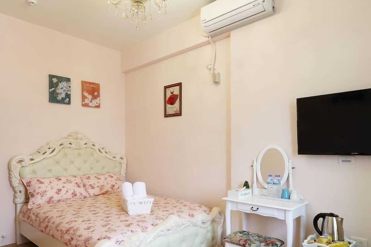 Quarto com cama, penteadeira com espelho, televisão e uma pequena geladeira.