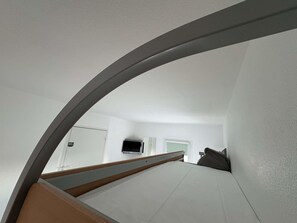 Um interior moderno com teto curvo, escada, TV de tela plana na parede e uma porta ao fundo.
