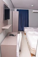 Quarto de hotel com duas camas, uma escrivaninha com telefone, TV fixada na parede e radiador.
