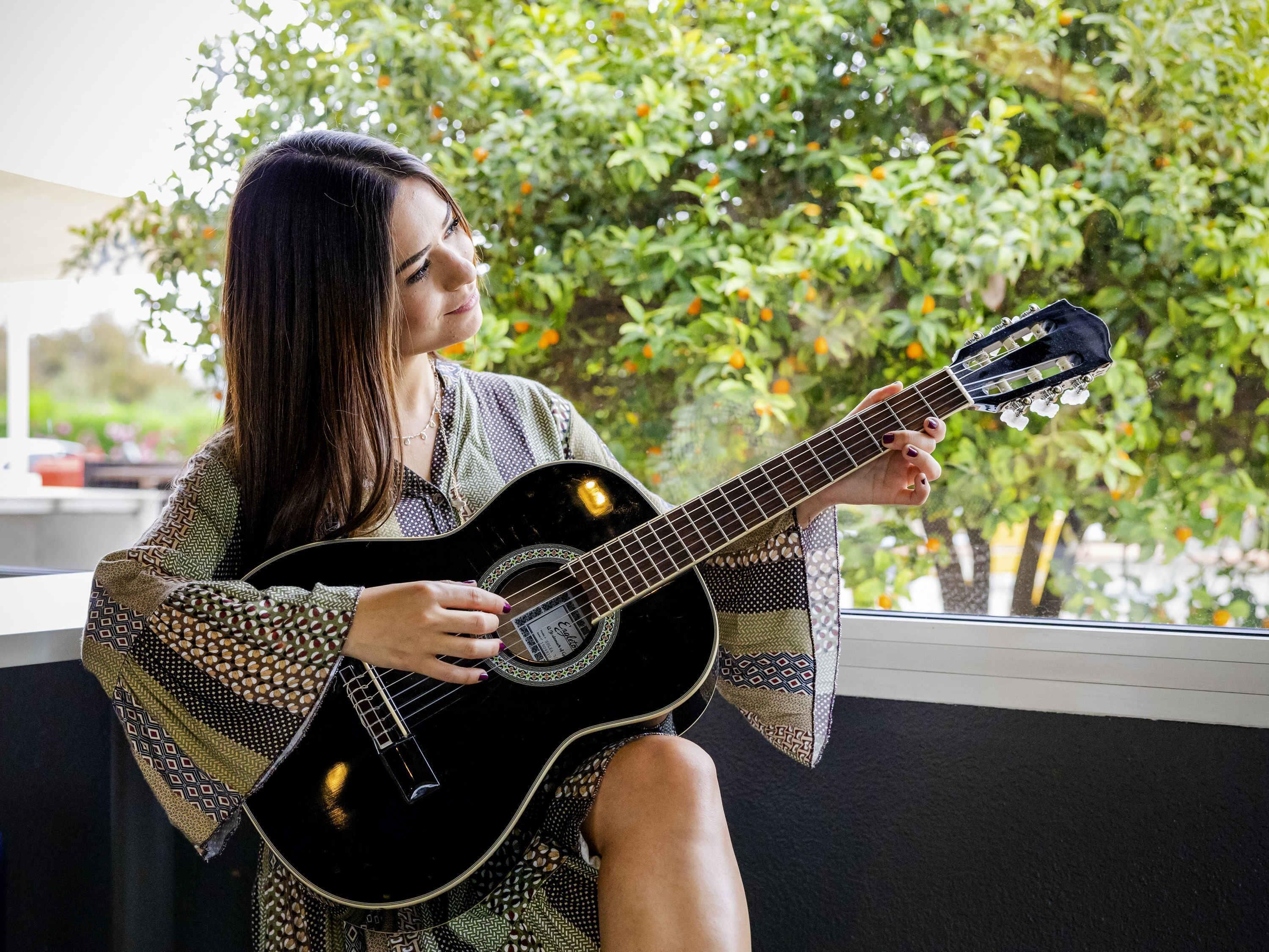 Uma pessoa tocando um violão preto com um xale estampado.