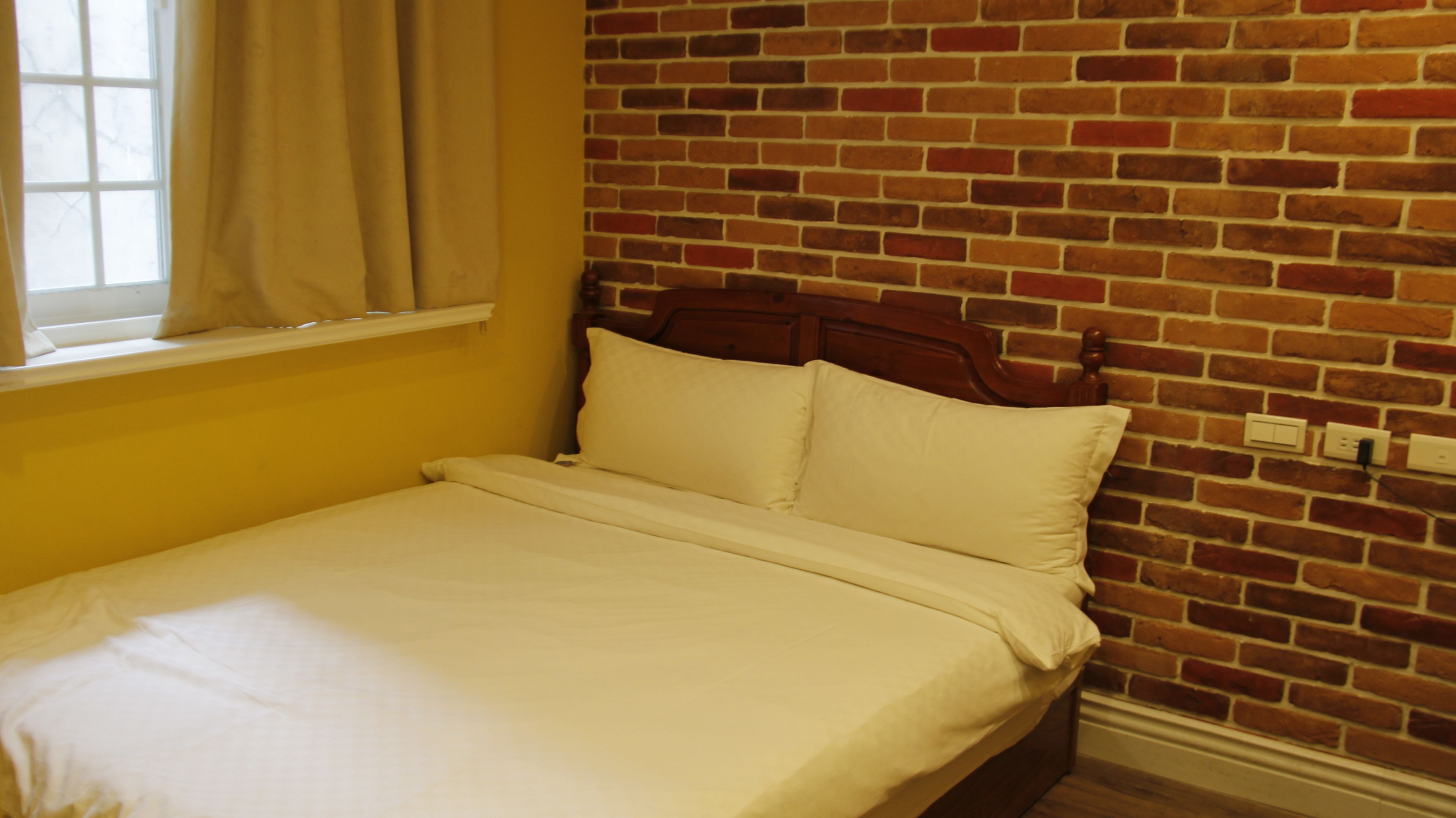 Uma cama de solteiro com cabeceira de madeira num quarto com parede de tijolos.