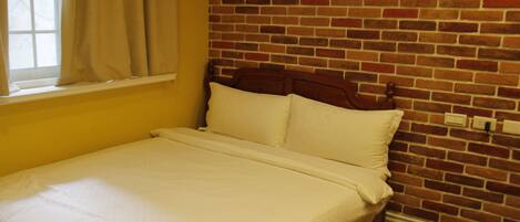 Uma cama de solteiro com cabeceira de madeira num quarto com parede de tijolos.