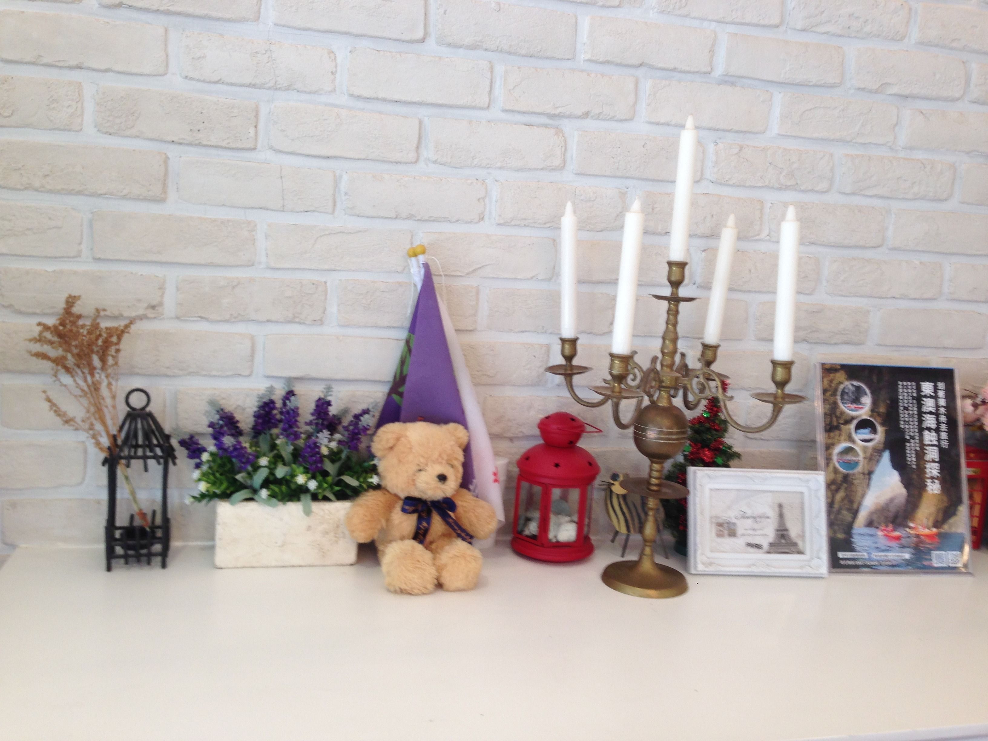Uma estante com um urso de pelúcia, um cone roxo, um lanterna vermelha, um candelabro e uma moldura com uma fotografia.