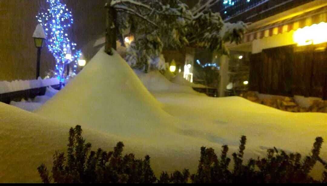 Paisagem coberta de neve com uma encosta nevada e um edifício com janelas iluminadas.