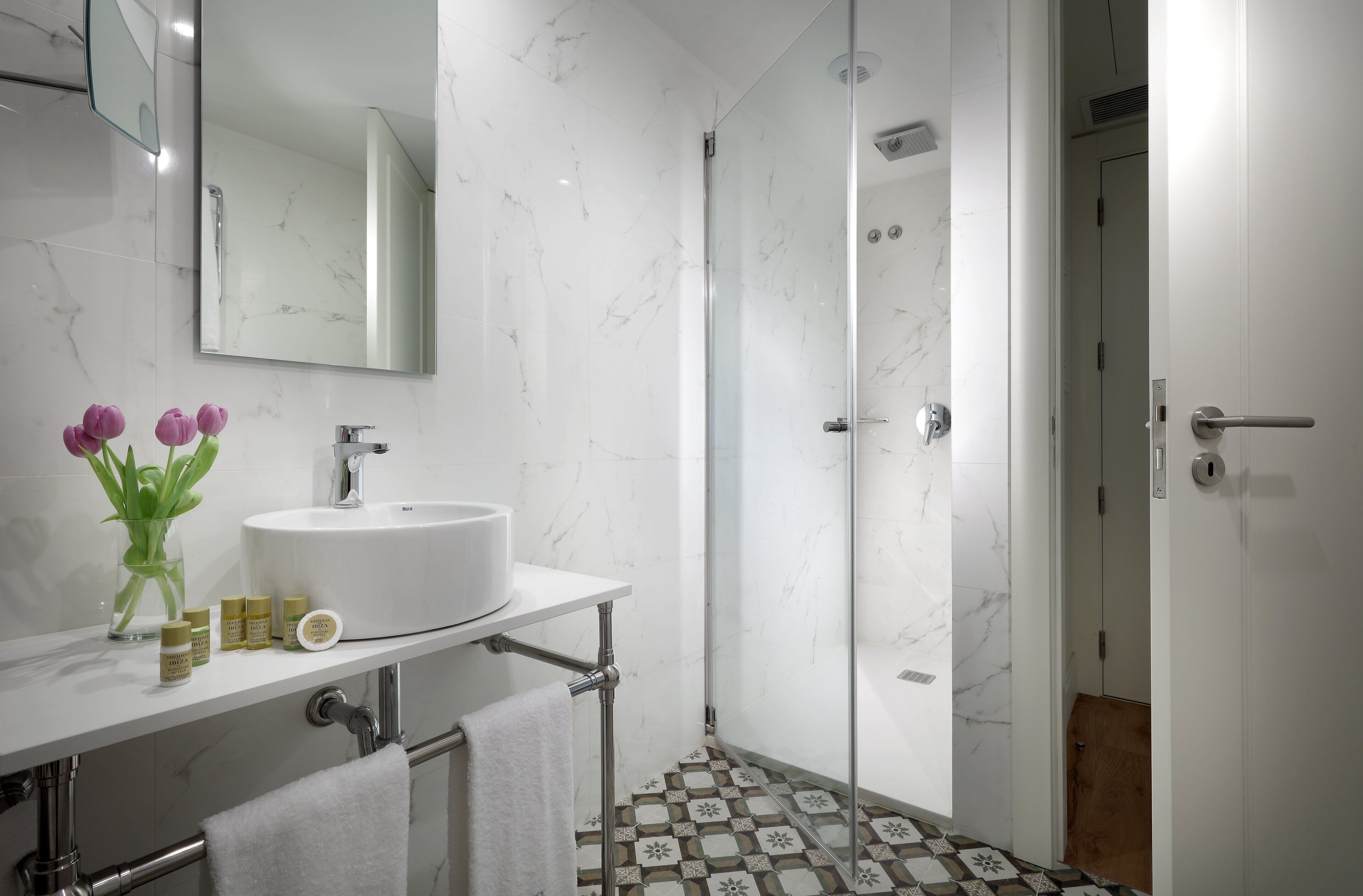 Uma casa de banho moderna com lavatório branco, espelho e chuveiro.