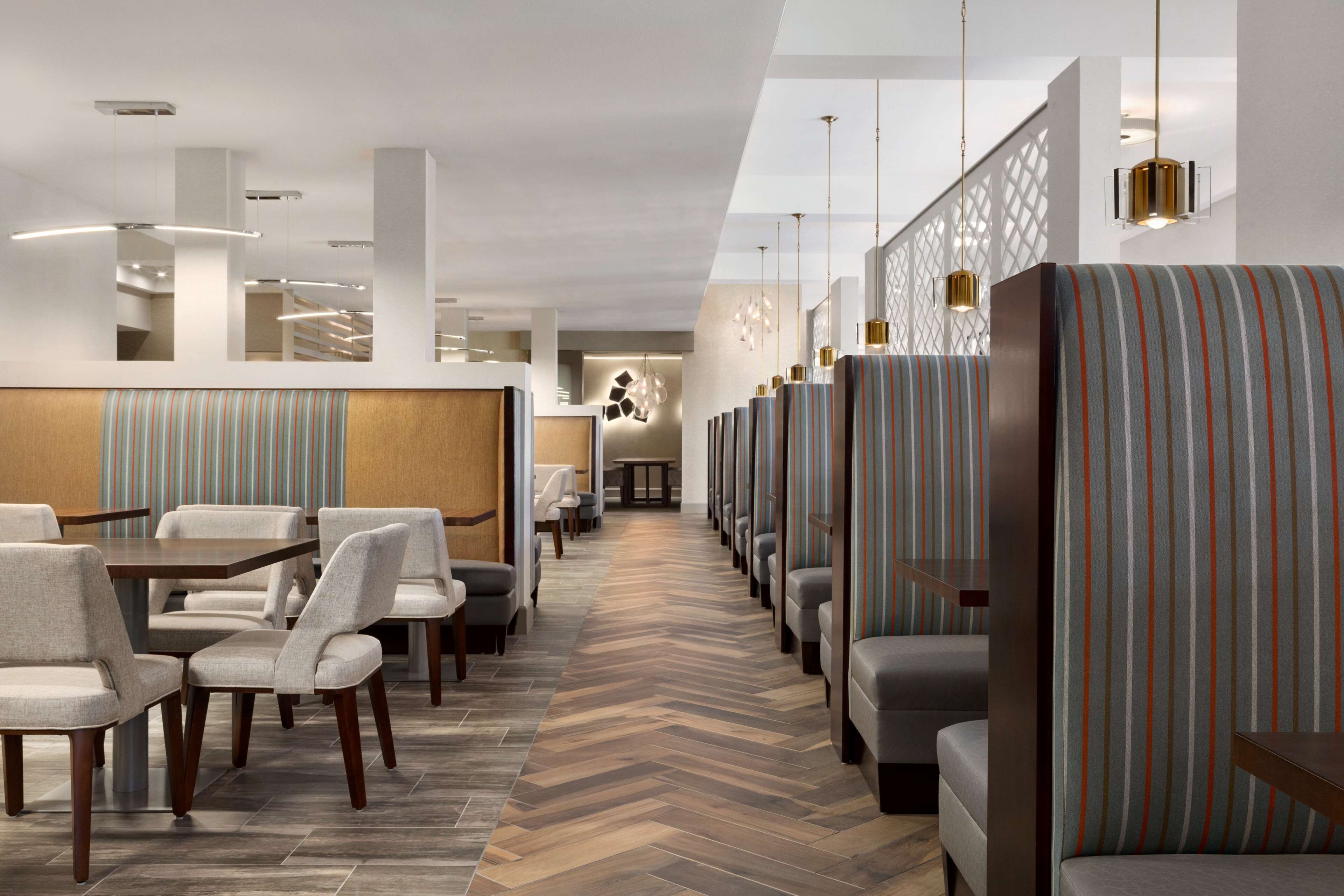 Um restaurante moderno com piso em padrão herringbone, cabines listradas e uma área de refeições central com mesas e cadeiras.