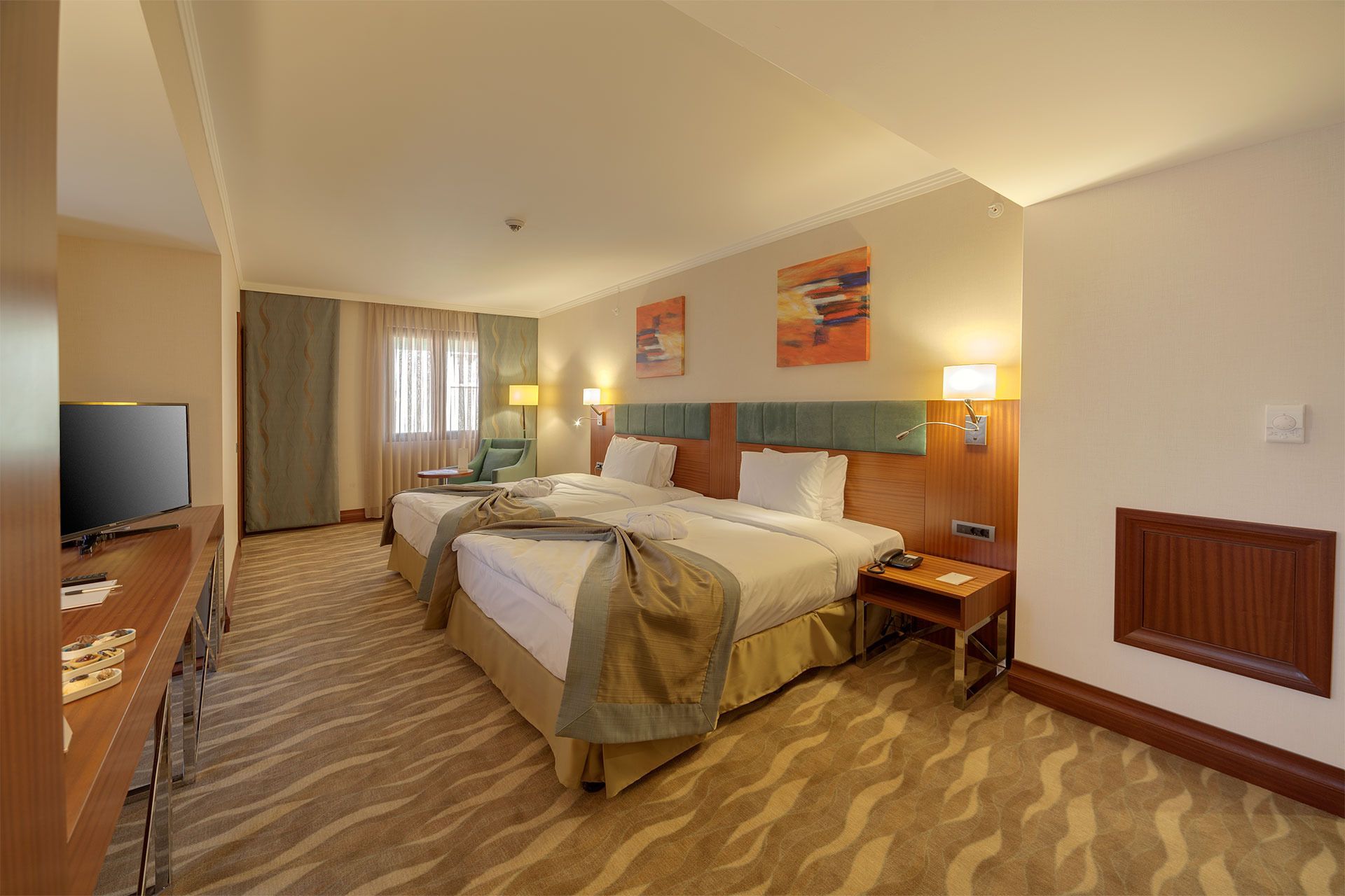 Quarto de hotel com duas camas, uma escrivaninha, televisão e janela com cortinas.