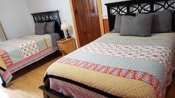 Duas camas de casal com colchas estampadas em floral, cabeceiras de madeira e mesas de cabeceira com abajures.