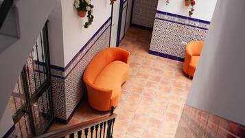 Escadaria que leva a um quarto com cadeiras laranja, piso ladrilhado e plantas em vasos.