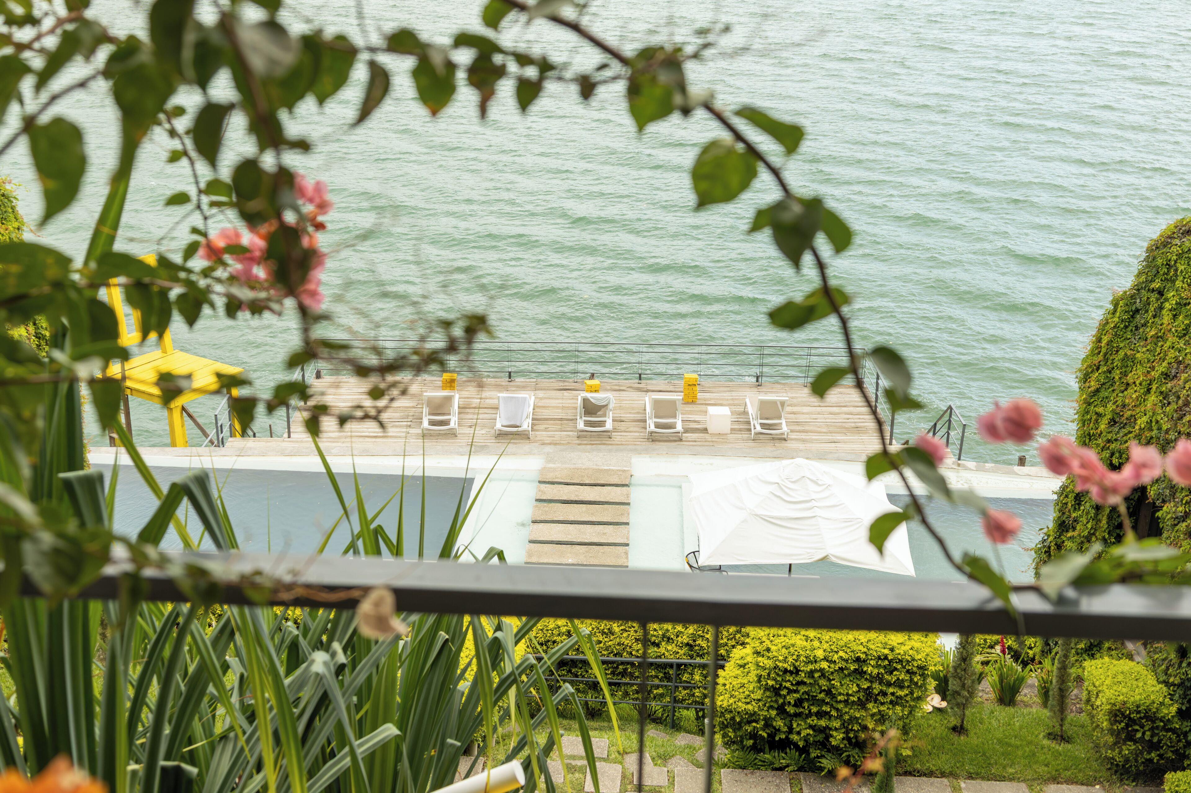 Vista de uma área de piscina com espreguiçadeiras e um toldo branco, cercada por vegetação e com vista para um corpo d'água.