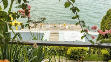 Vista de uma área de piscina com espreguiçadeiras e um toldo branco, cercada por vegetação e com vista para um corpo d'água.