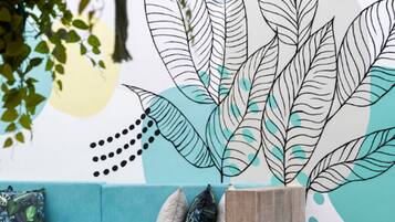 Um interior moderno com um sofá azul-turquesa, almofadas estampadas e um mural de folhas estilizadas.