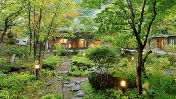 Um jardim japonês tradicional com um caminho, pedras e um edifício com fachada de madeira.