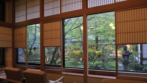 Um quarto em estilo japonês tradicional, com tatames, portas deslizantes de madeira e grandes janelas com vista para um jardim.