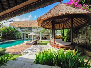 Um resort com piscina, construções com telhados de palha e vegetação exuberante.