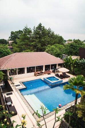 Piscina com deck ladrilhado, cadeiras de descanso e área de estar coberta.