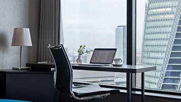Quarto de hotel moderno com uma escrivaninha, laptop e vista para a paisagem urbana.