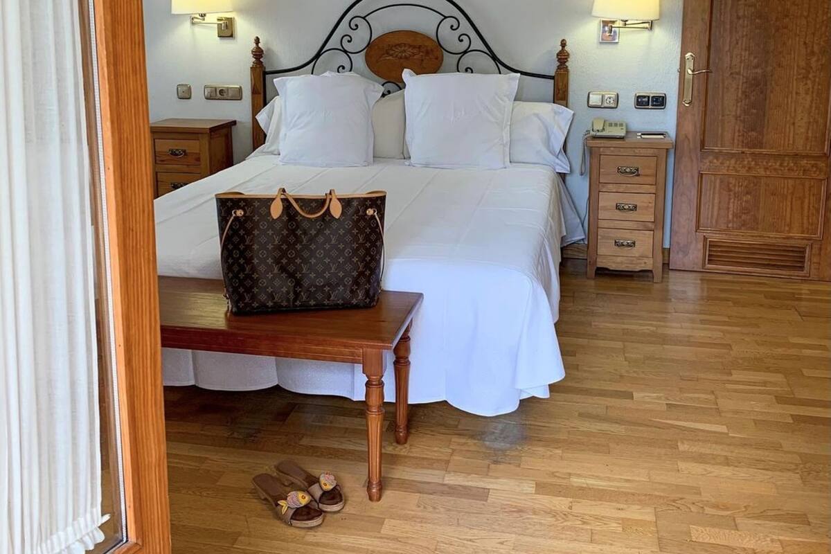 Quarto bem arrumado com cama, mesas de cabeceira, um criado-mudo de madeira, um guarda-roupa de madeira e uma bolsa na cama.