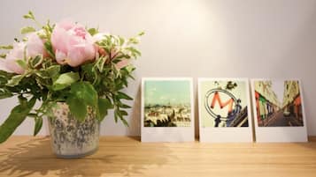 Um vaso com flores cor-de-rosa sobre uma superfície de madeira, três quadros na parede ao fundo.
