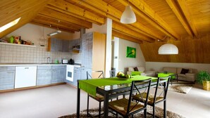 Cozinha moderna com vigas de madeira, área de jantar com toalha de mesa verde e sala de estar com sofá e planta.