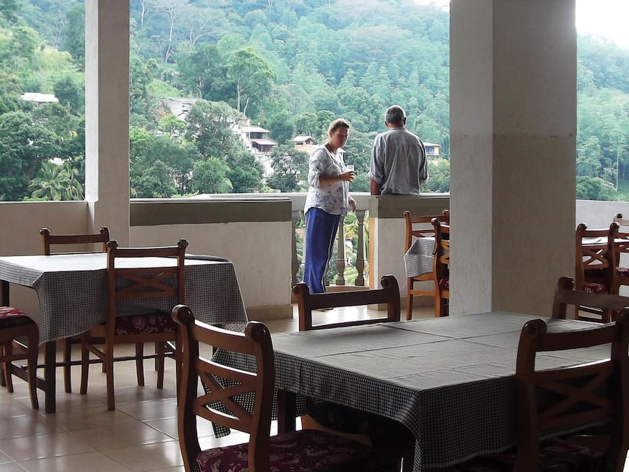 Uma área de refeições com mesas e cadeiras, uma varanda com vista para uma paisagem verde exuberante.