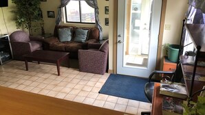 Uma sala de estar com sofá, mesa de centro e porta que dá para o exterior.