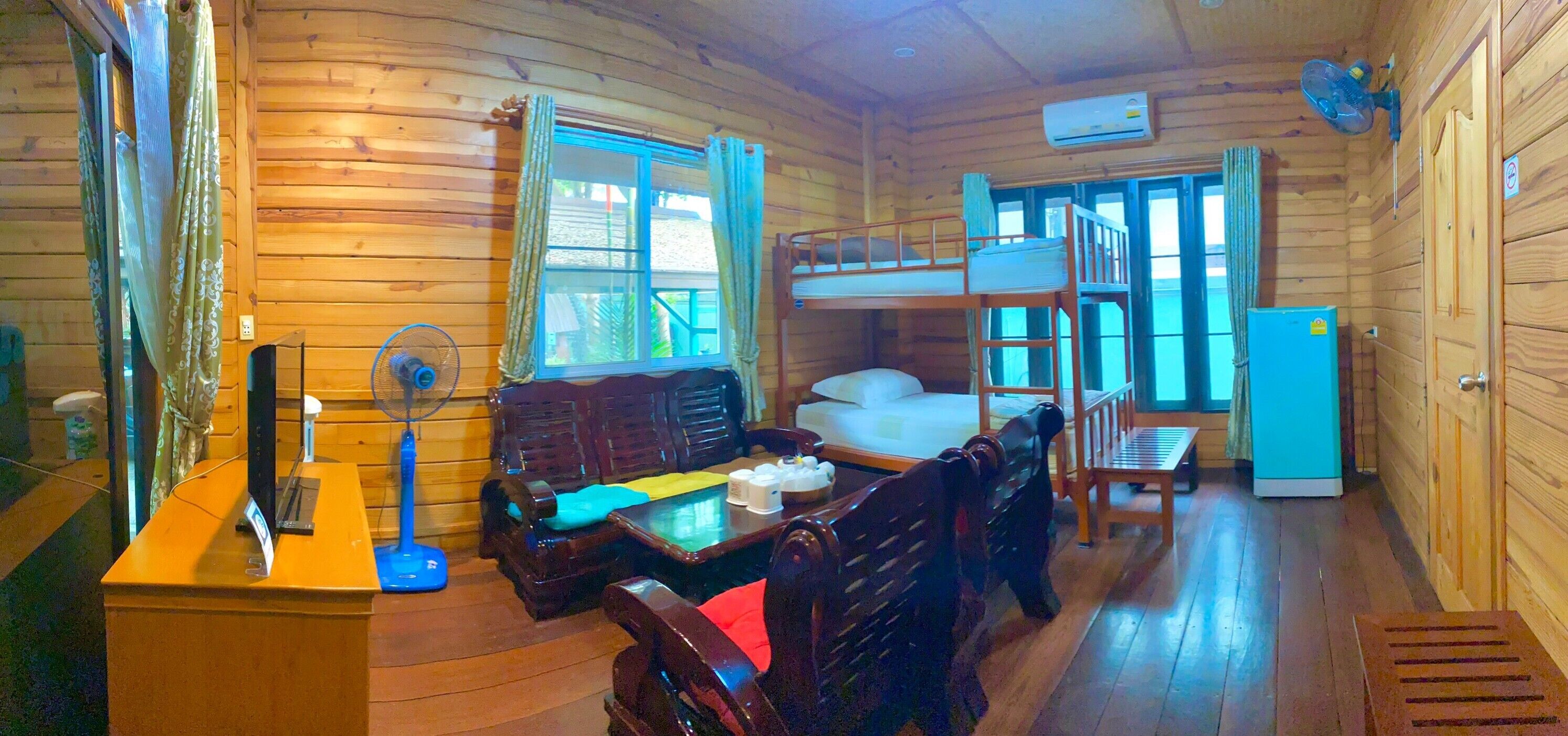 Uma cabana de madeira com beliches, uma escrivaninha, um ventilador e uma geladeira.