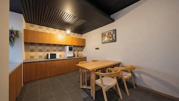 Cozinha compacta com armários de madeira, micro-ondas e cafeteira. Há uma mesa de jantar com cadeiras e um teto com design em ripas.