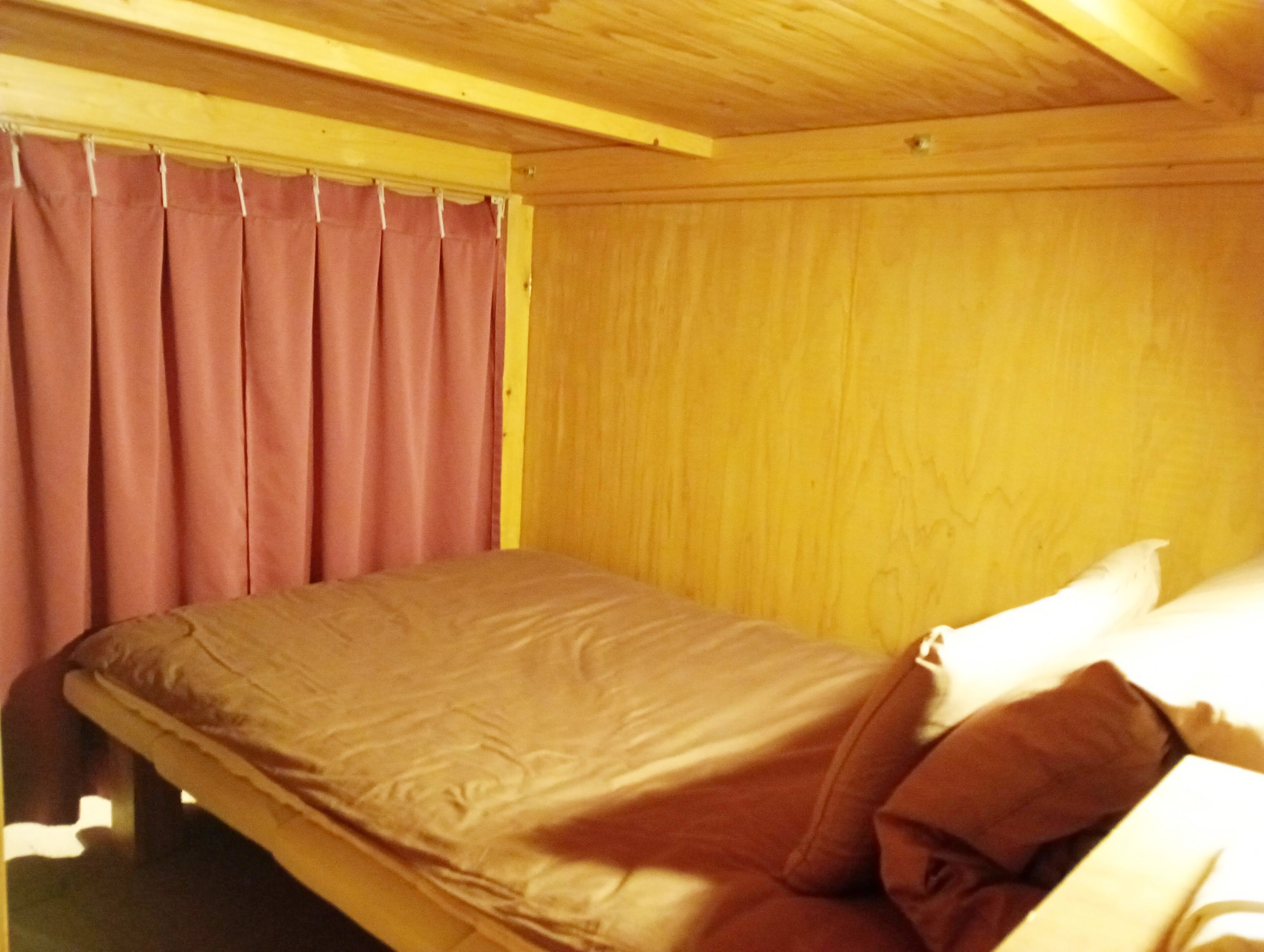 Uma cama de solteiro num quarto com paredes de madeira e uma cortina.