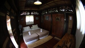 Quarto tradicional com duas camas, paredes de madeira e ventilador de teto.