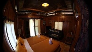 Quarto com teto de madeira, cama, mesinha e janela com cortinas.