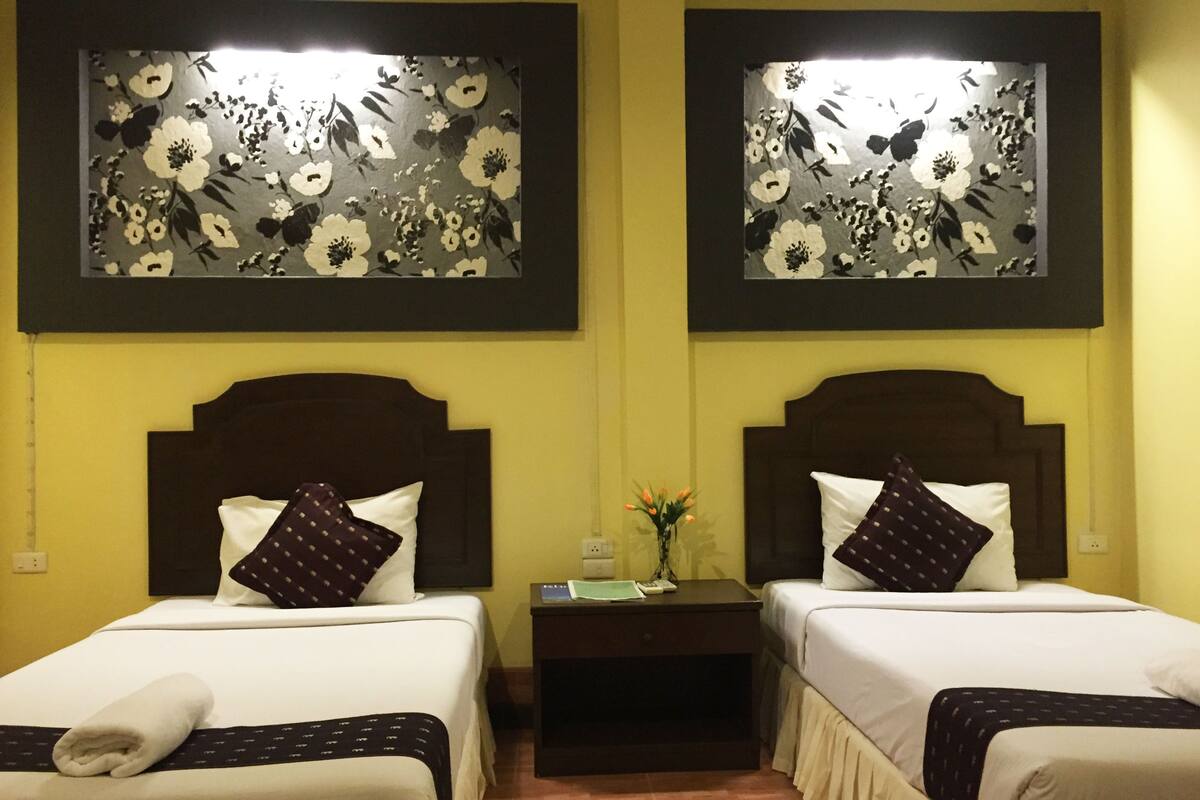 Quarto de hotel com duas camas, cada uma com cabeceira, mesa de cabeceira com um vaso de flores e uma obra de arte pendurada na parede acima das camas.