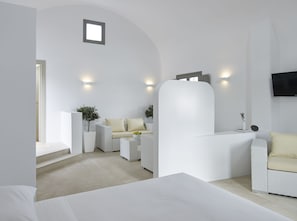 Quarto de hotel moderno e minimalista com sofá, uma mesa pequena e televisão na parede.